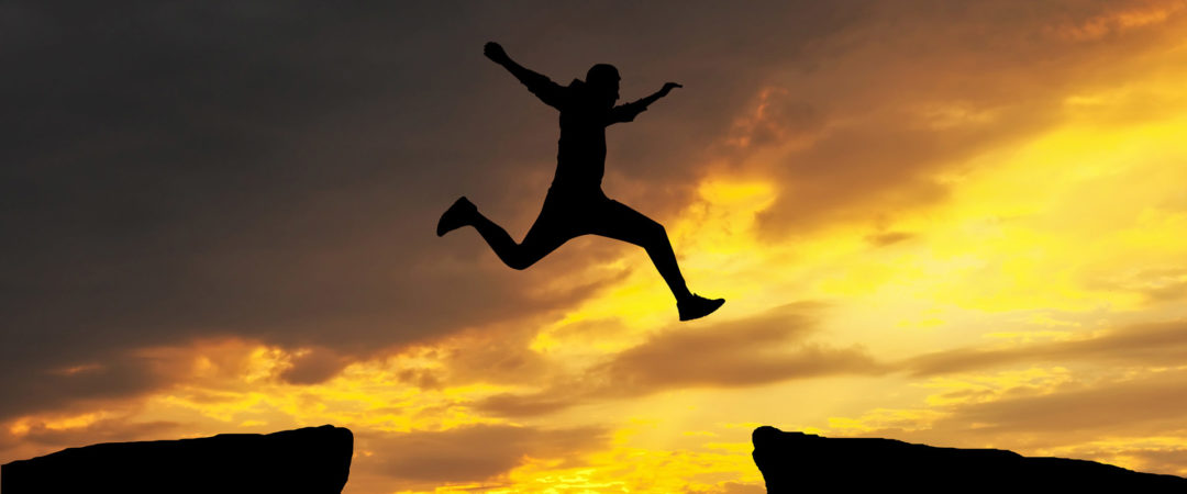 Man jumping across the gap from one rock to cling to the other. Man ...
